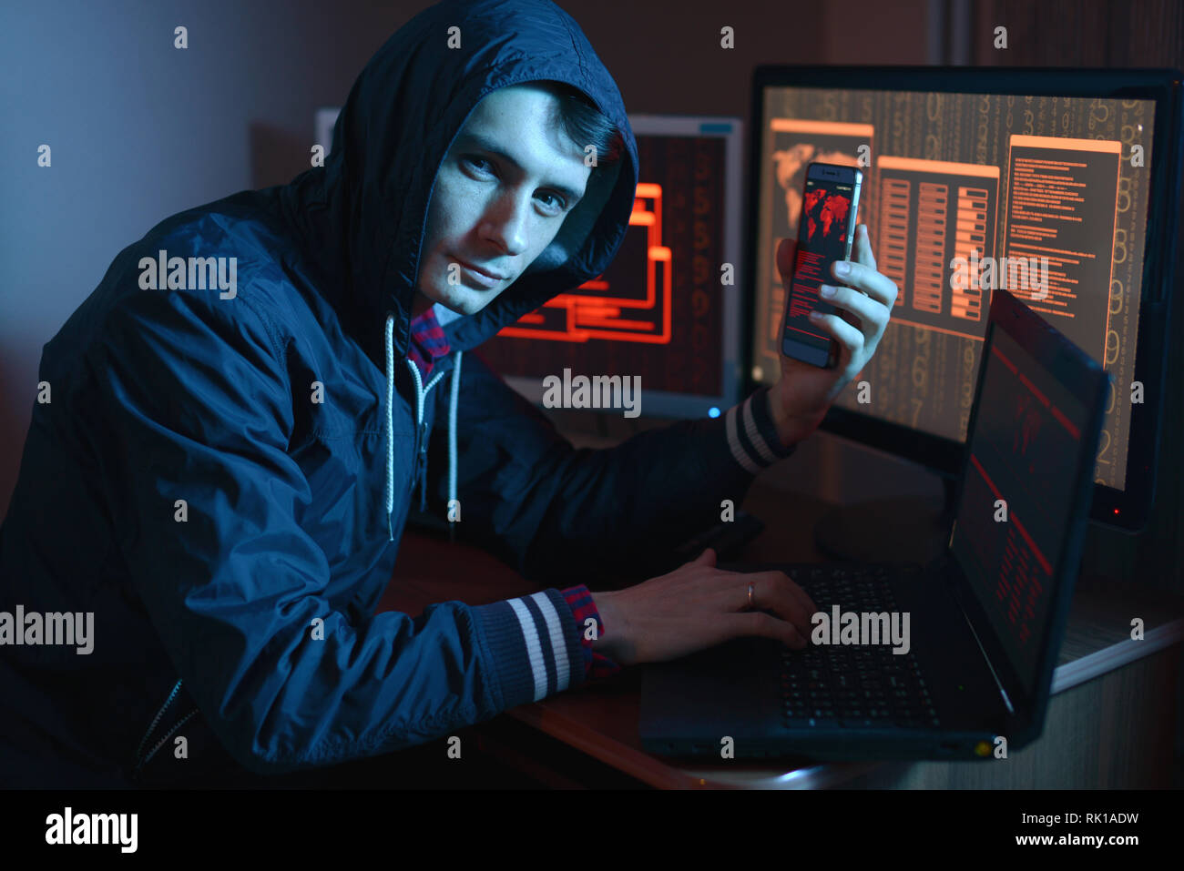 Male hacker in the hood holding the phone in his hands trying to hack ...