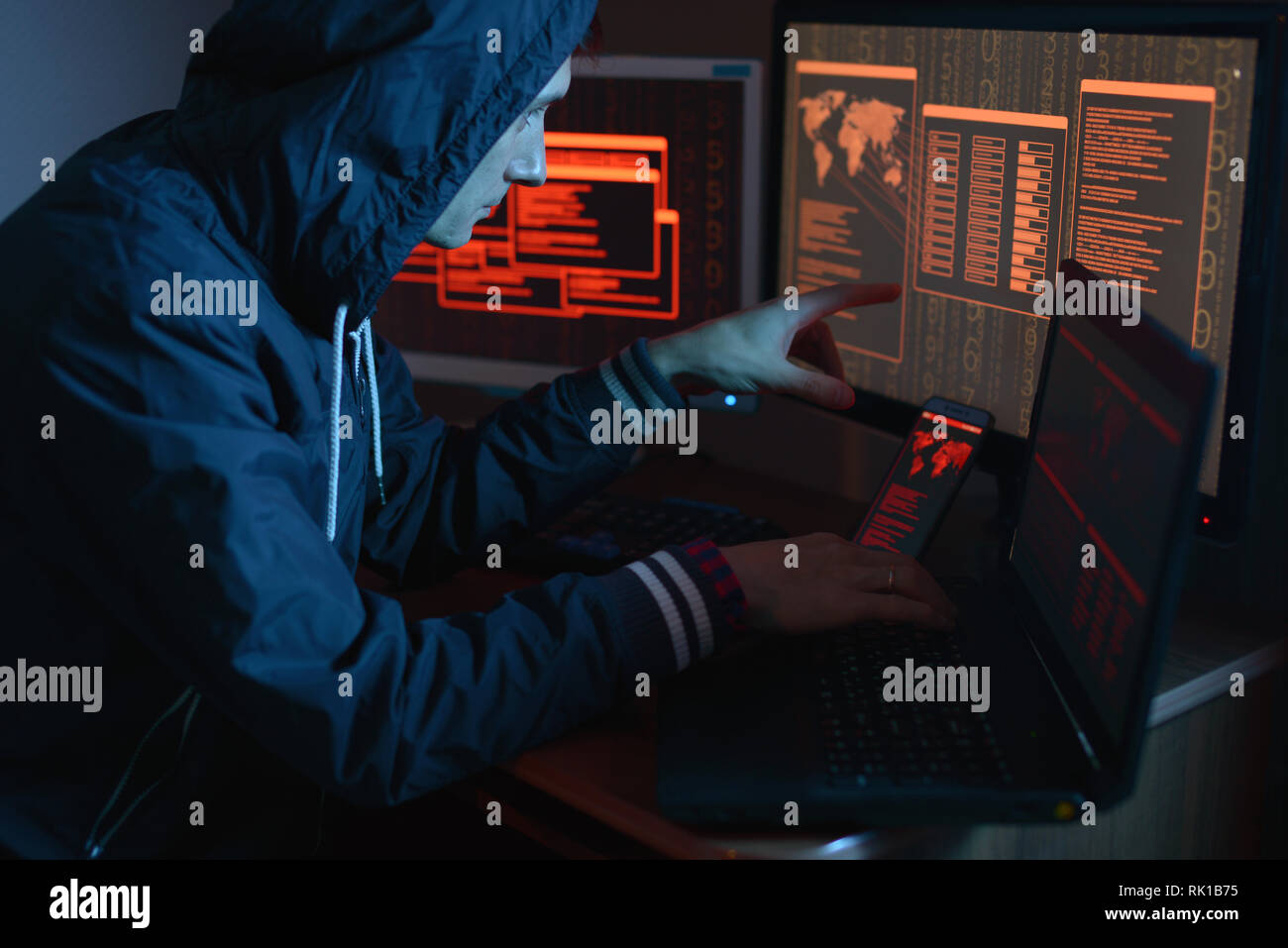The male hacker in the hood is pointing his finger at the display ...