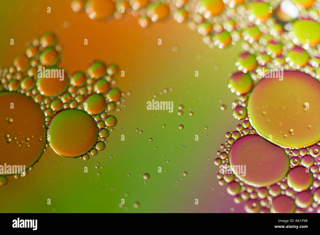 A closeup of oil droplets on a water surface with a colored background ...