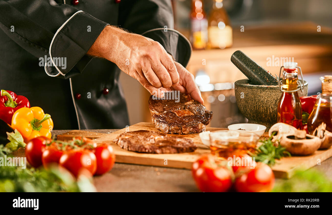 Chef seasoning a raw steak for grilling surrounded by fresh ingredients ...