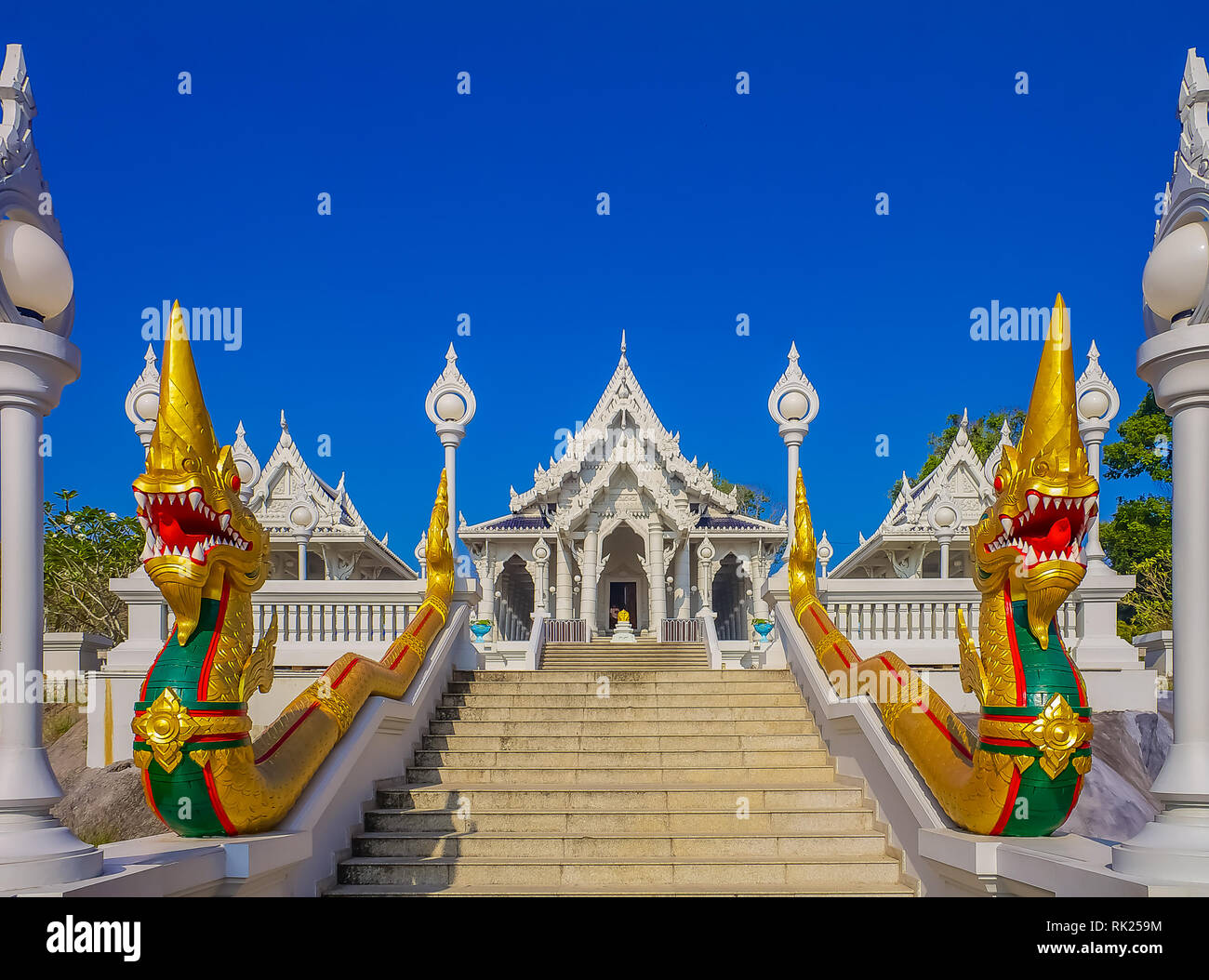 Ornate and colorful golden naga statues in front of the white Thai ...