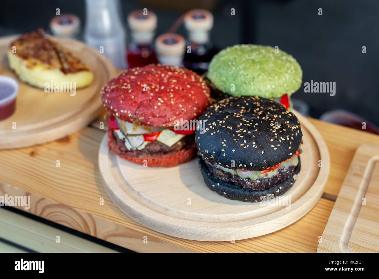 Three tasty bright multicolored beef burgers on wooden counter at food ...
