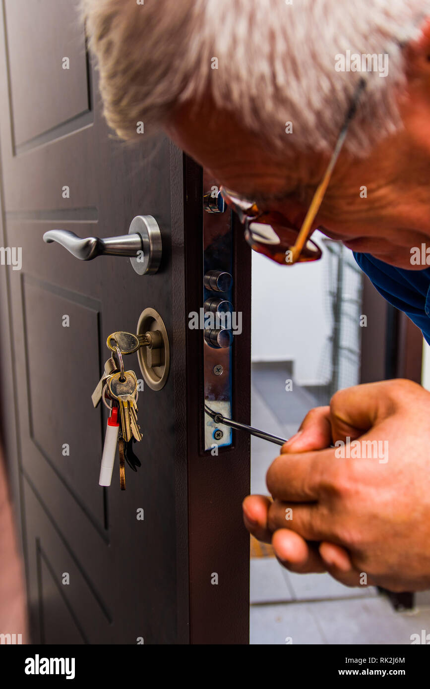 Old age handyman is fixing the door lock with tool Stock Photo - Alamy