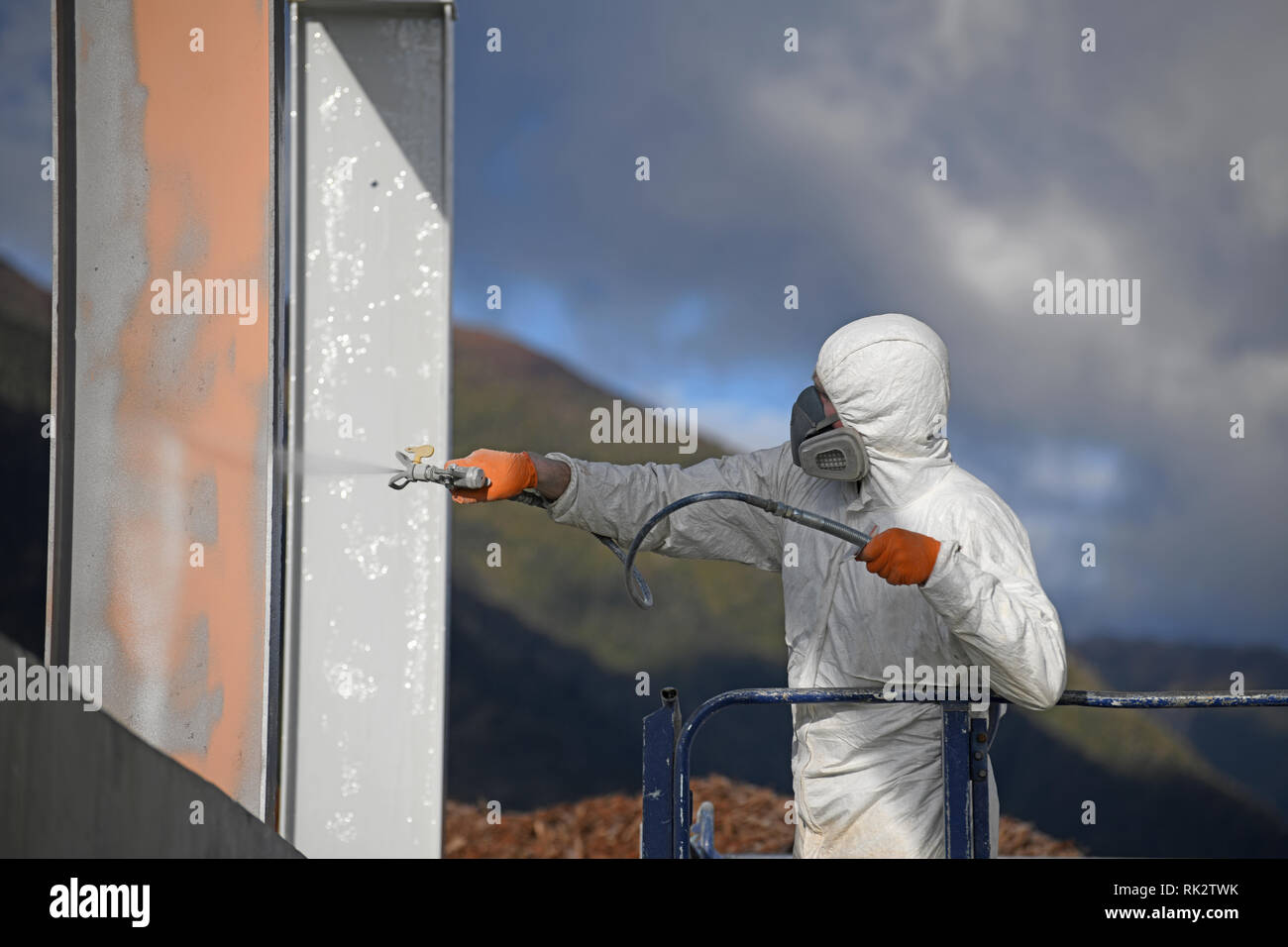 A tradesman spray paints steel beams with primer at a construction site ...