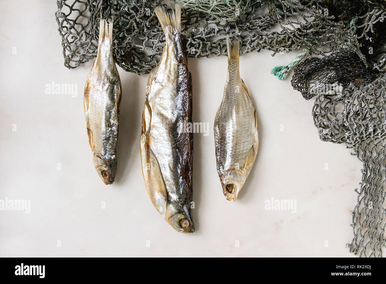 Dried fish or stockfish on fishing nets over white marble background ...