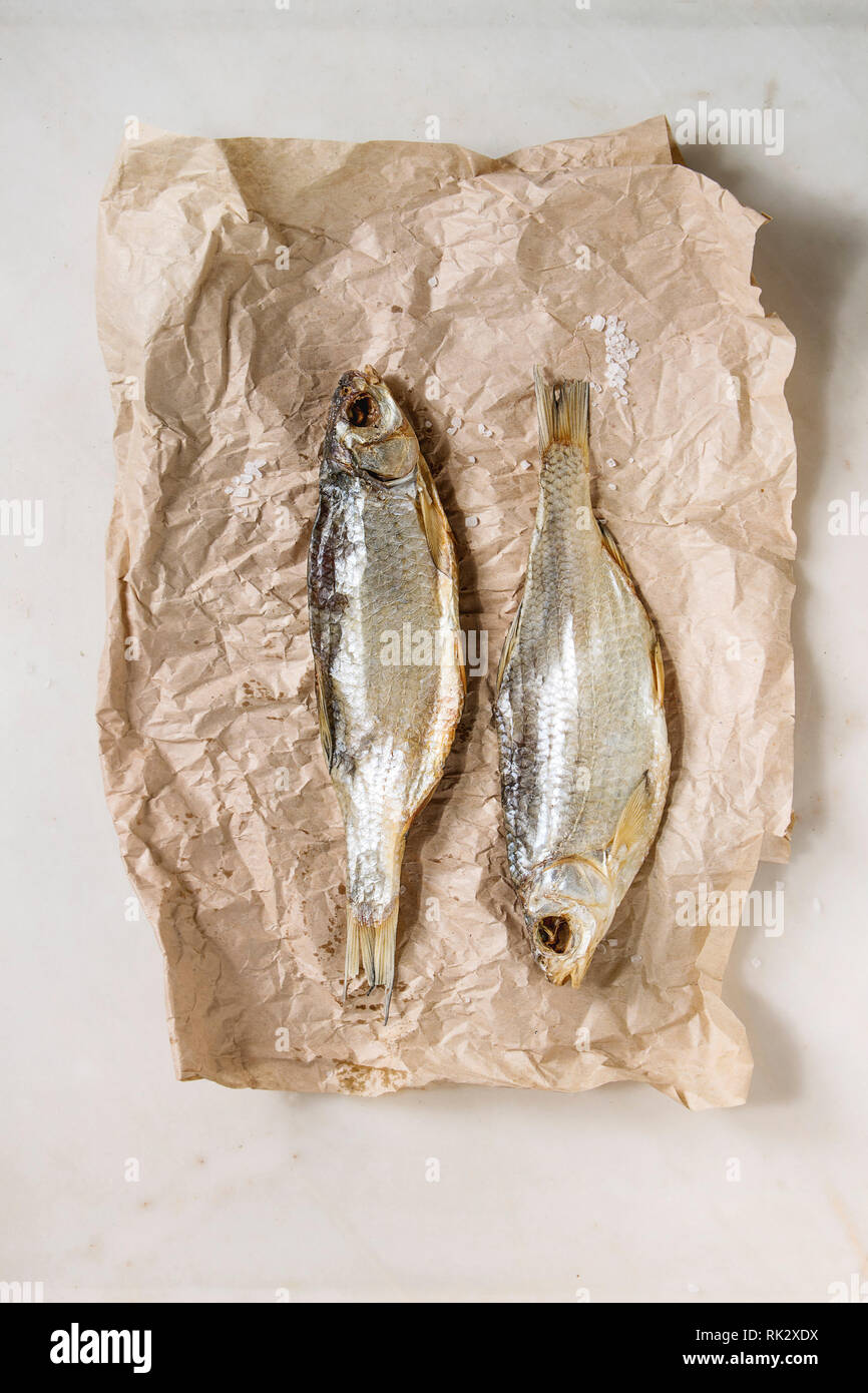 Dried fish or stockfish on crumpled paper over white marble background ...