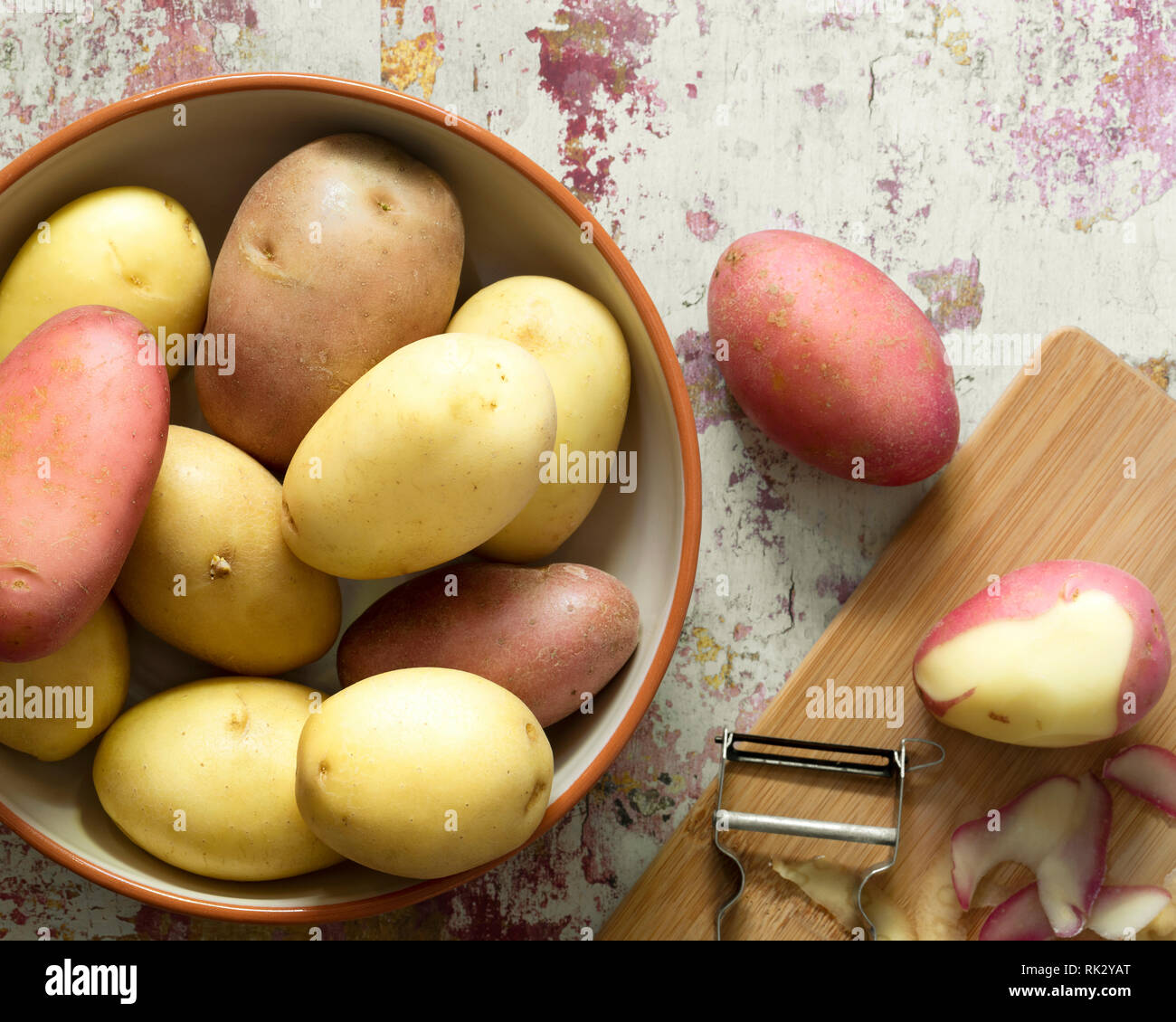 Washed red and white potatoes in a bowl and one with the skin partially ...