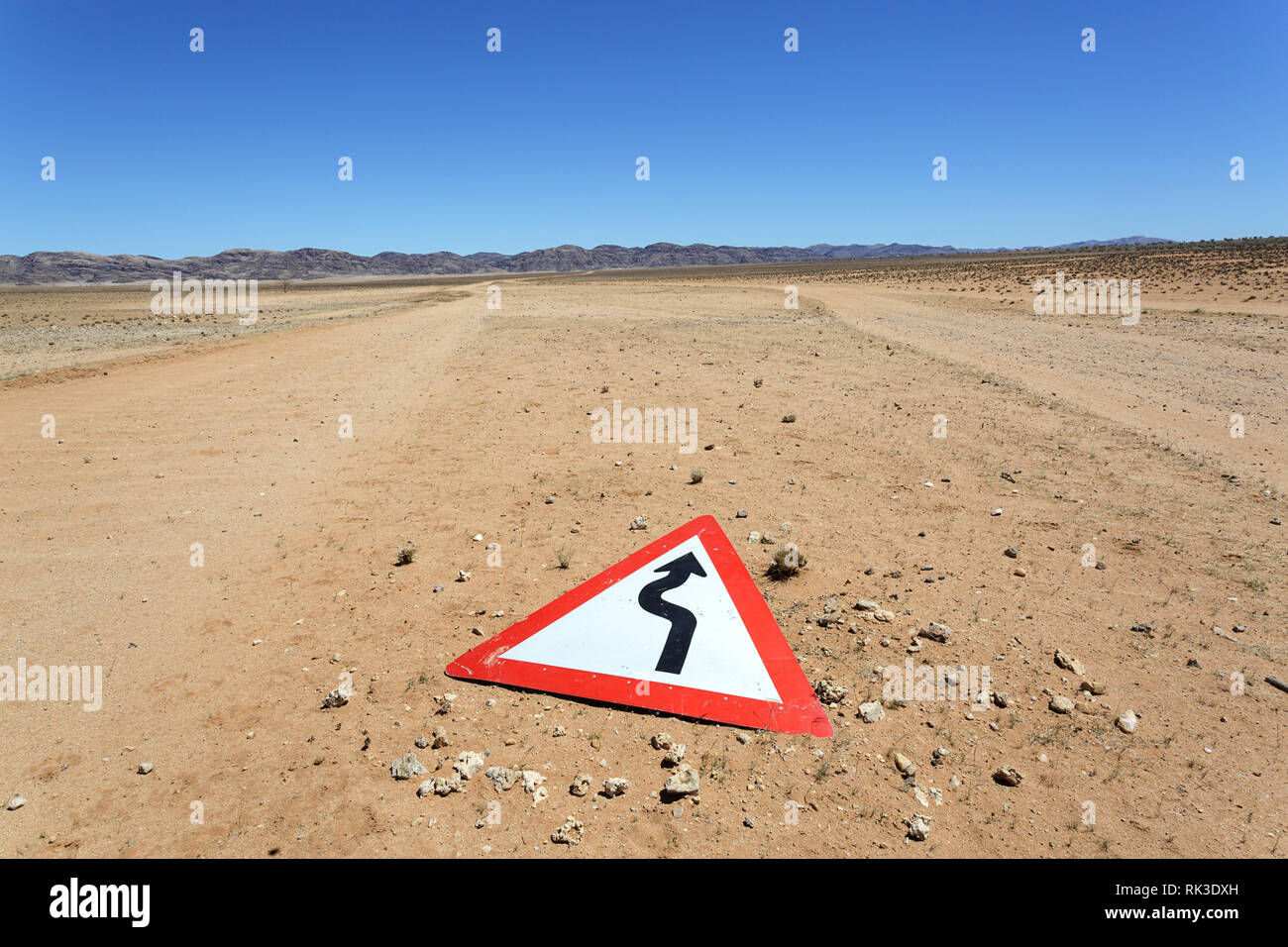 Warning sign sharp turns on the road lying on the ground in Namib ...