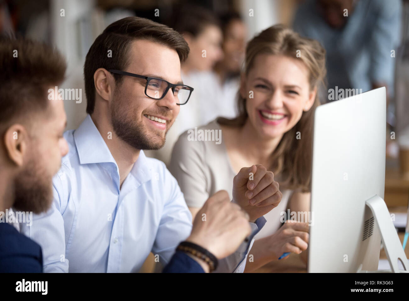 Happy colleagues looking at computer screen talking laughing working ...