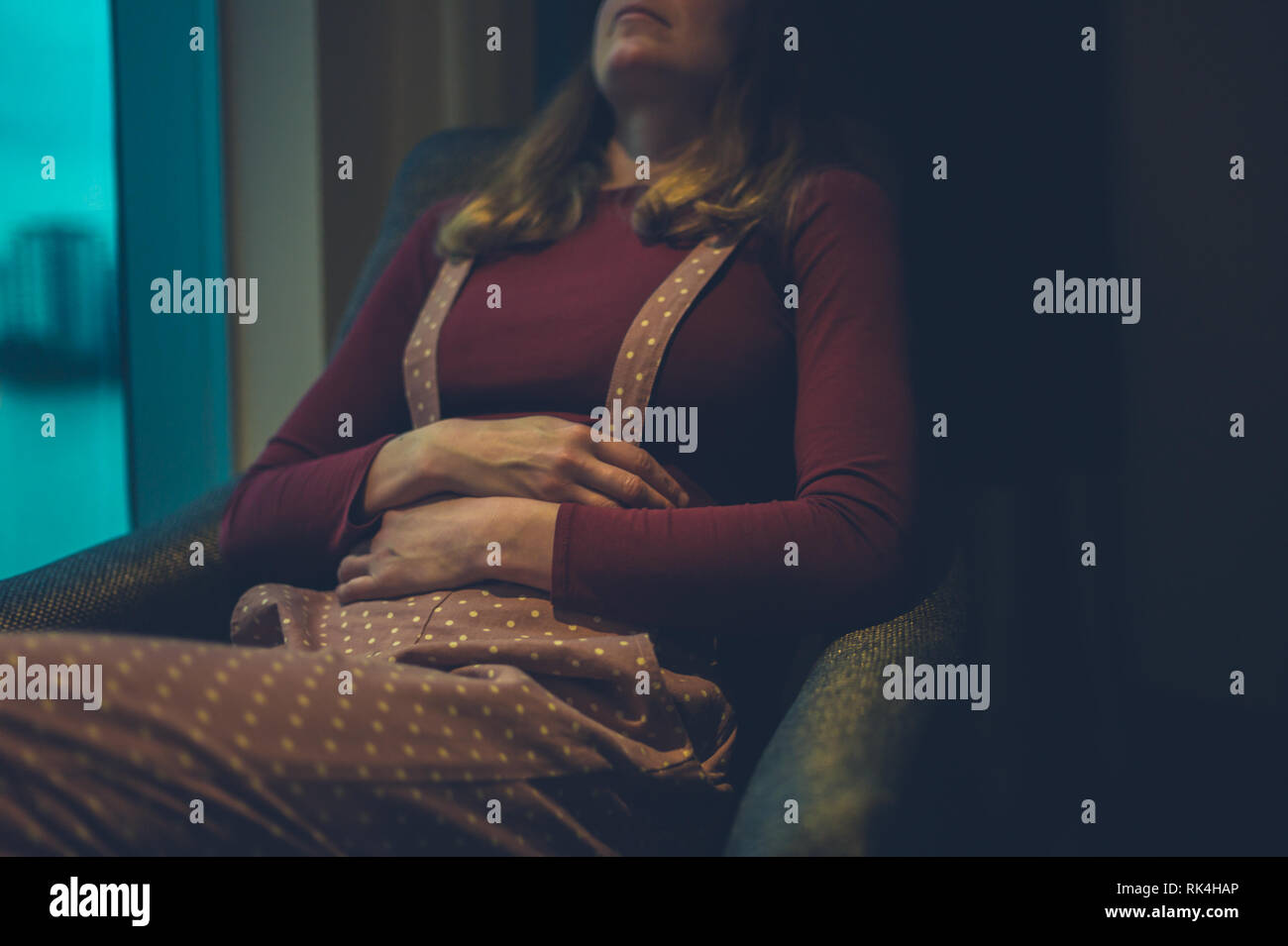 A young woman with a stomach ache is sitting by the window in the city ...