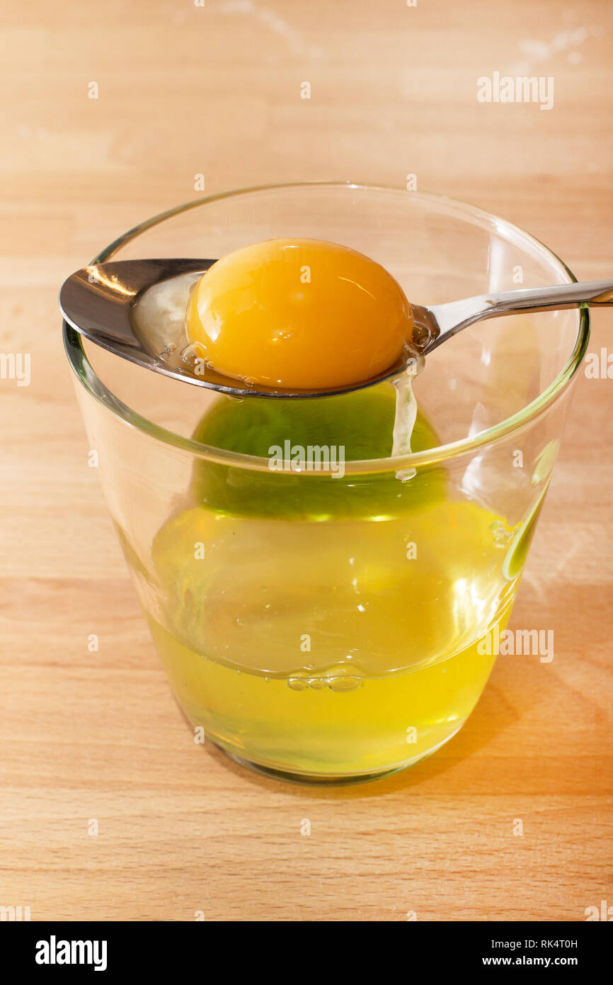 Close up raw yellow yolk separation in spoon and glass with white of ...