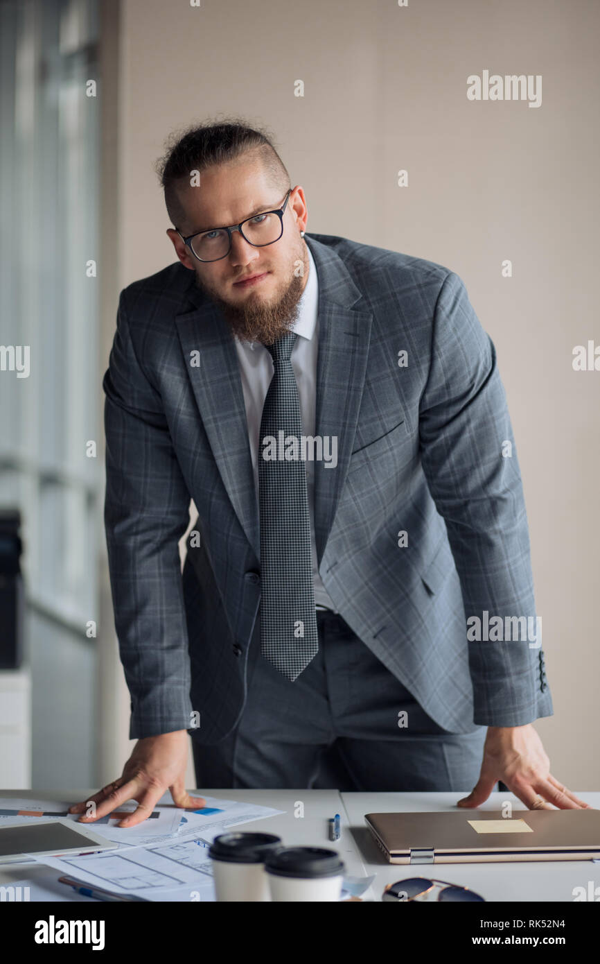 confident strict bearded red-haired businessman is leaning on the table ...