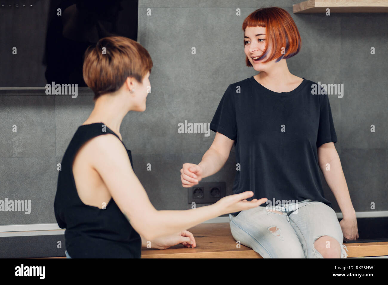 Two young cheerful female friends discussing something in the living ...