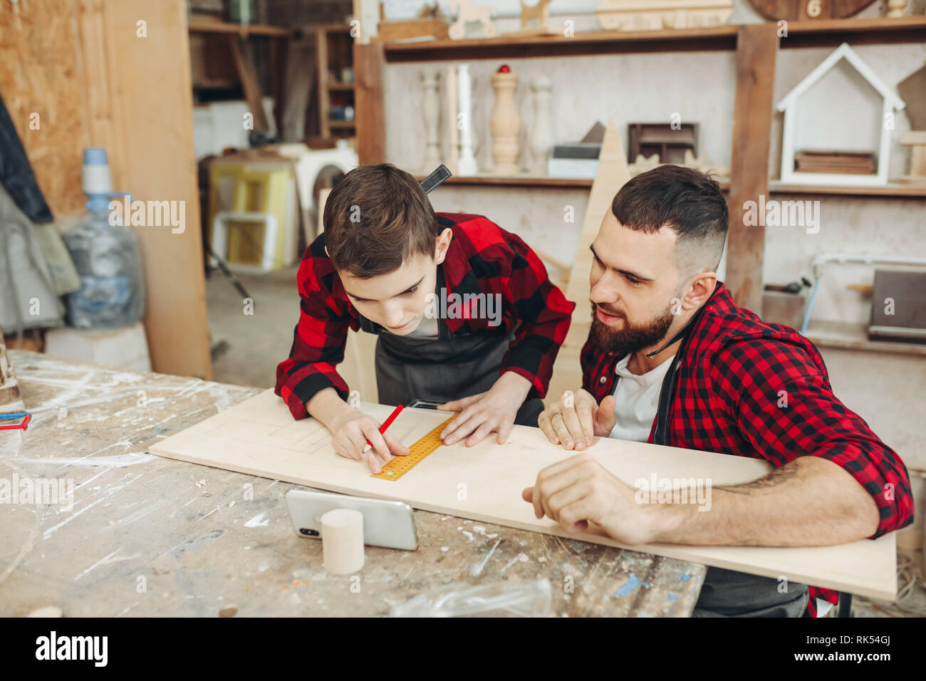 Focused craftsman and his little follower boy are measuring wood using ...