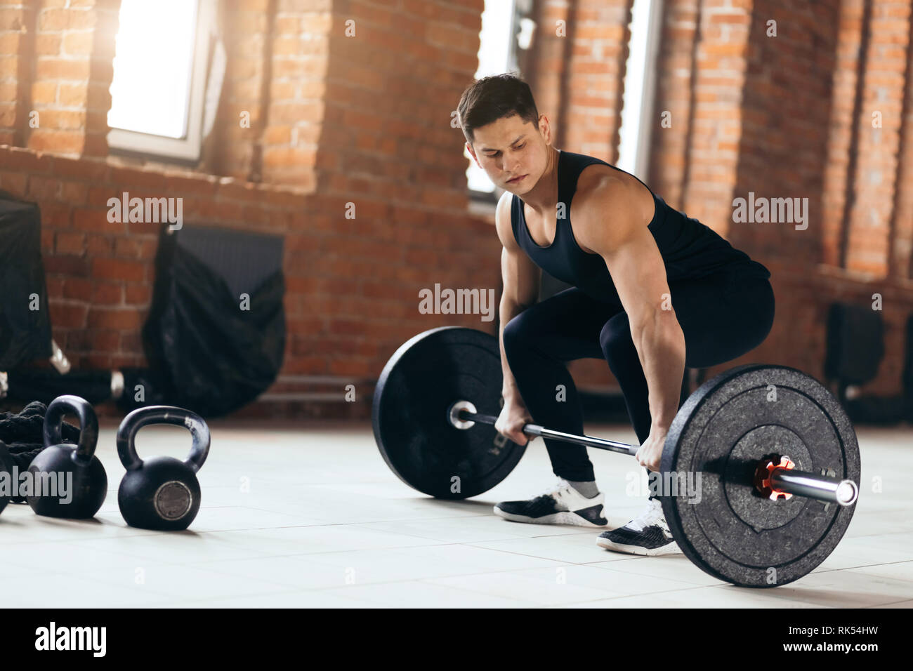 young ambitious bodybuilder is holding barbell. full length side view ...