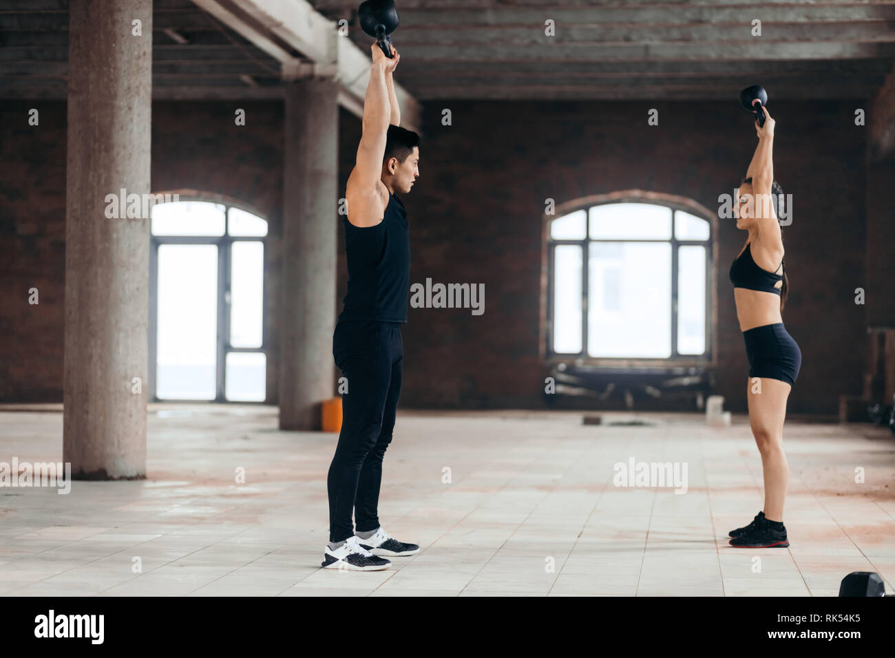 Fit man and woman holding kettlebells over their heads. full length ...