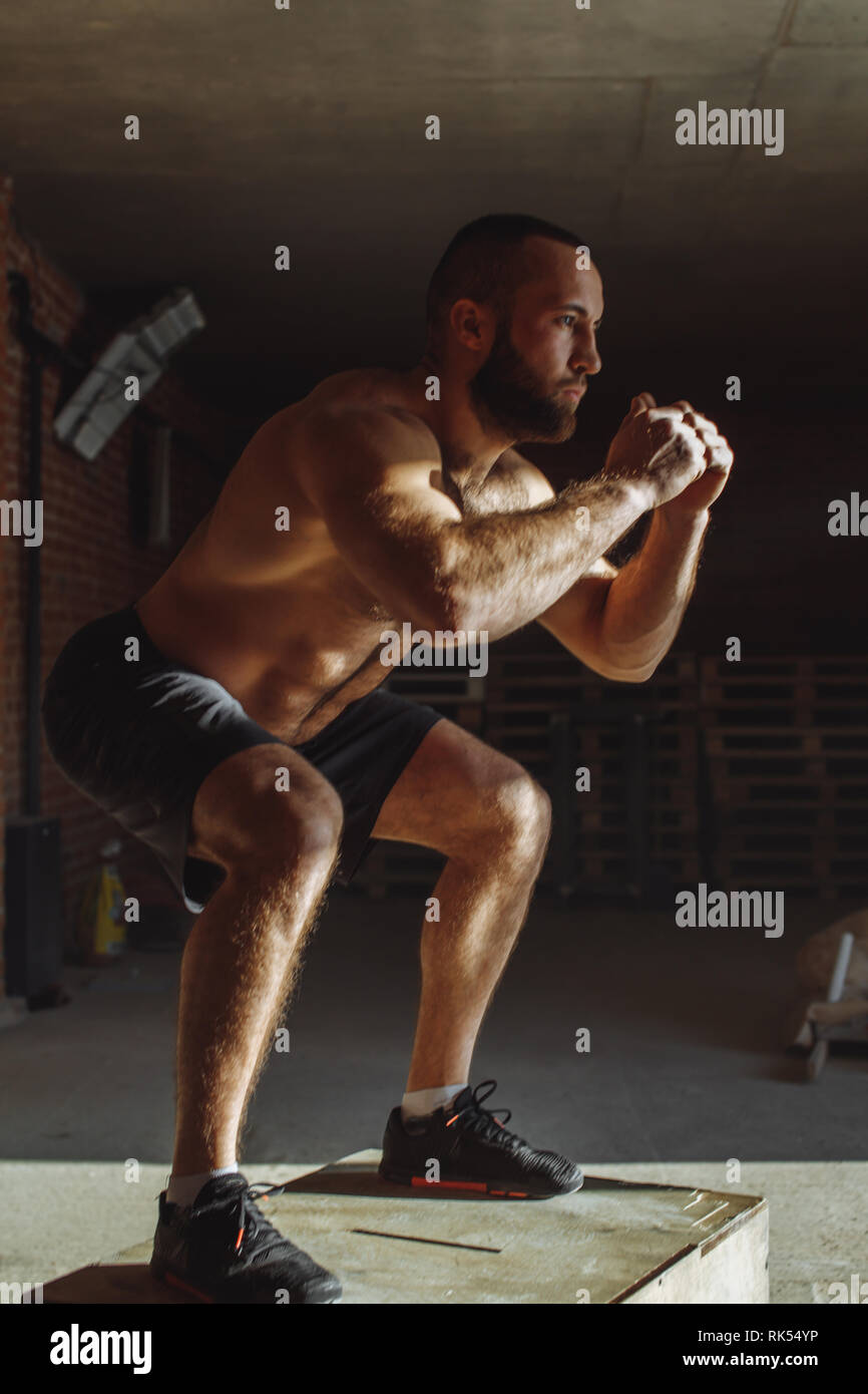 Determined young man jumping onto a box as part of exercise routine ...