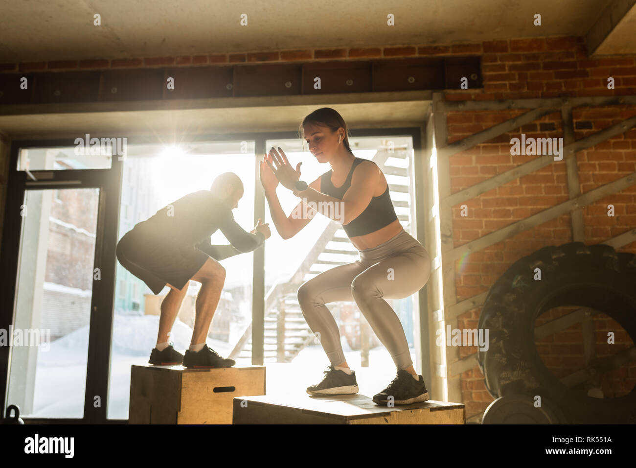 Fit caucasian couple doing squats on boxes in a crossfit style gym ...