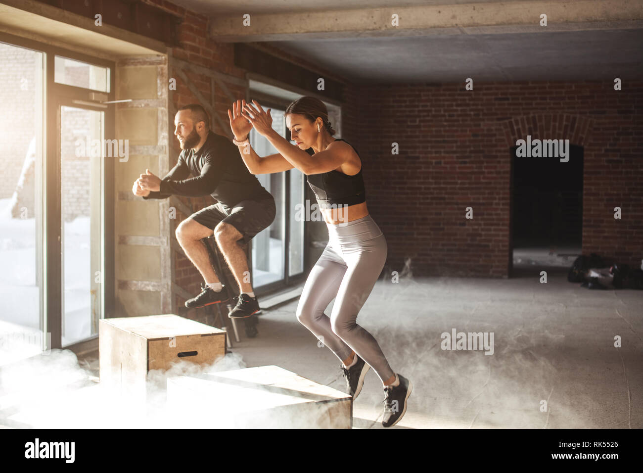 Fit caucasian couple doing squats on boxes in a crossfit style gym ...