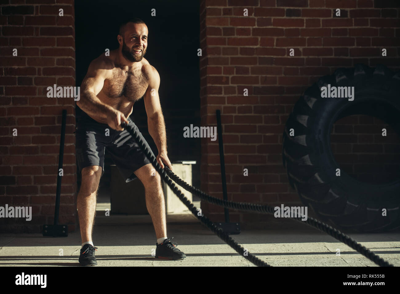 Muscular powerful determined man training with rope in functional ...