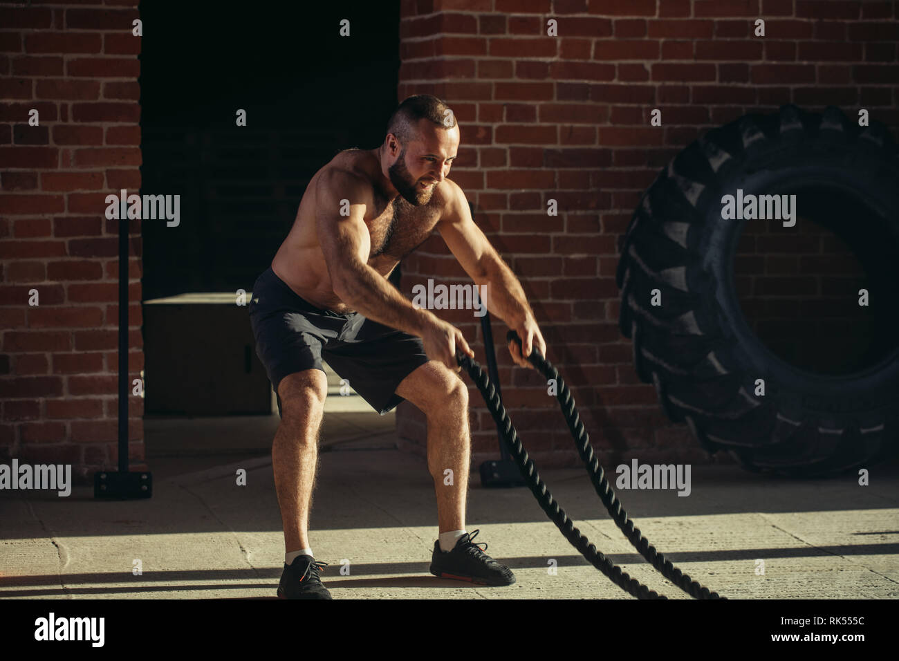 Athletic young man with battle rope doing exercise in functional ...
