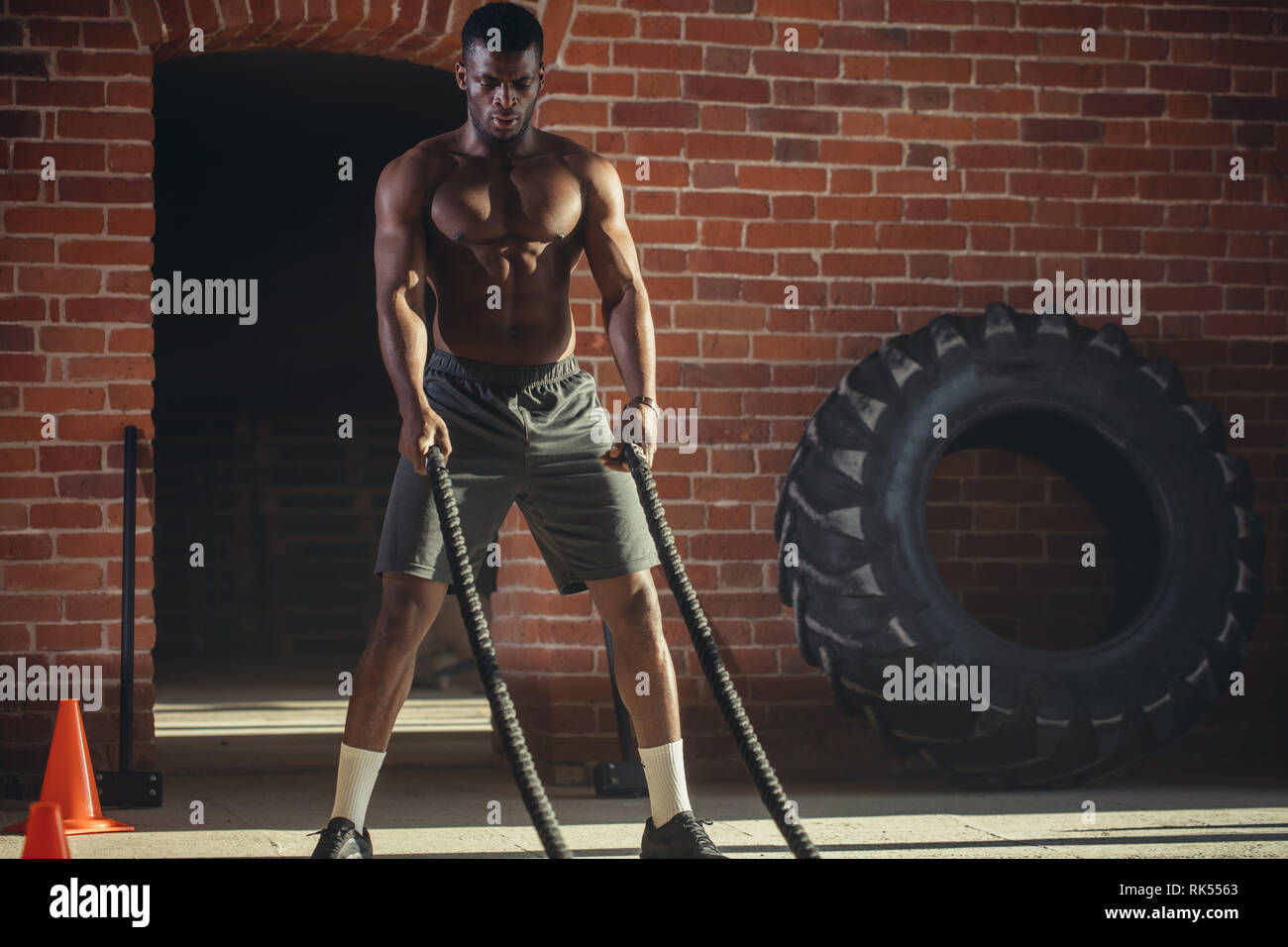 Afro american bodybuilder with battle rope in cross-fit training centre ...