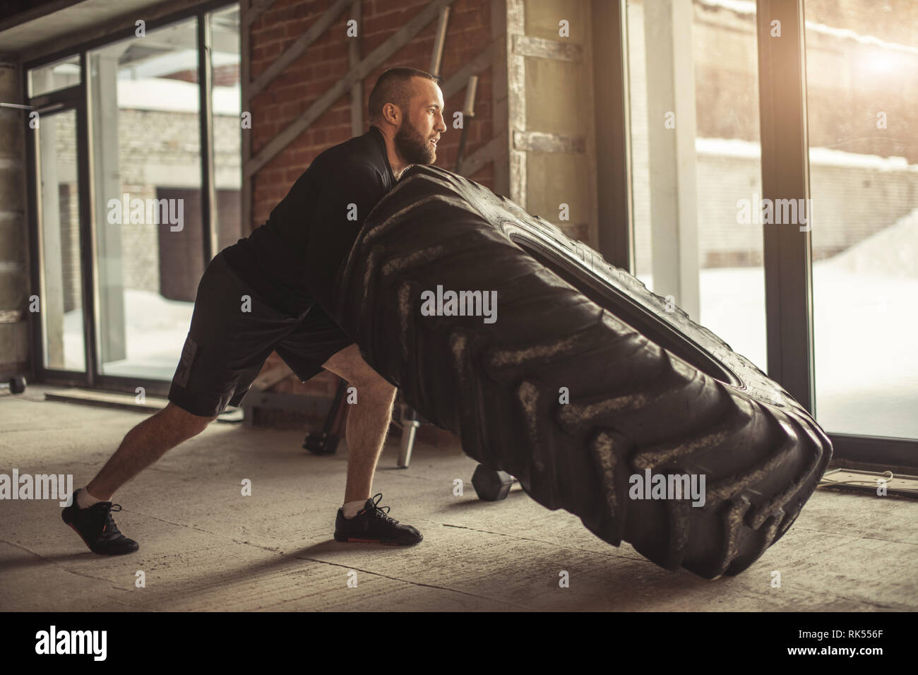 Young muscular bearded man using heavy tire in gym as improvised ...