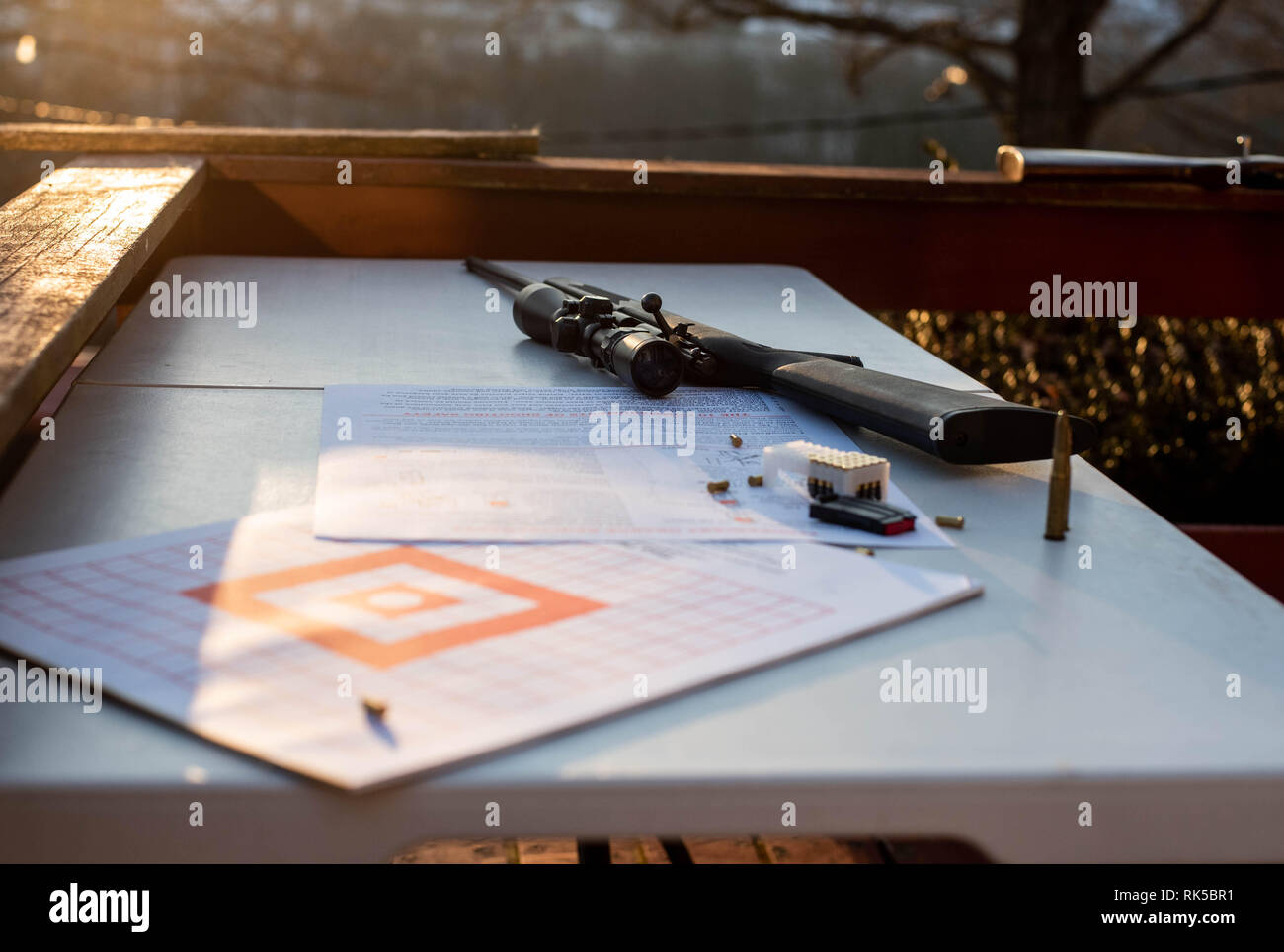 A 22-caliber rifle sits on a table with bullets around it as the sun ...