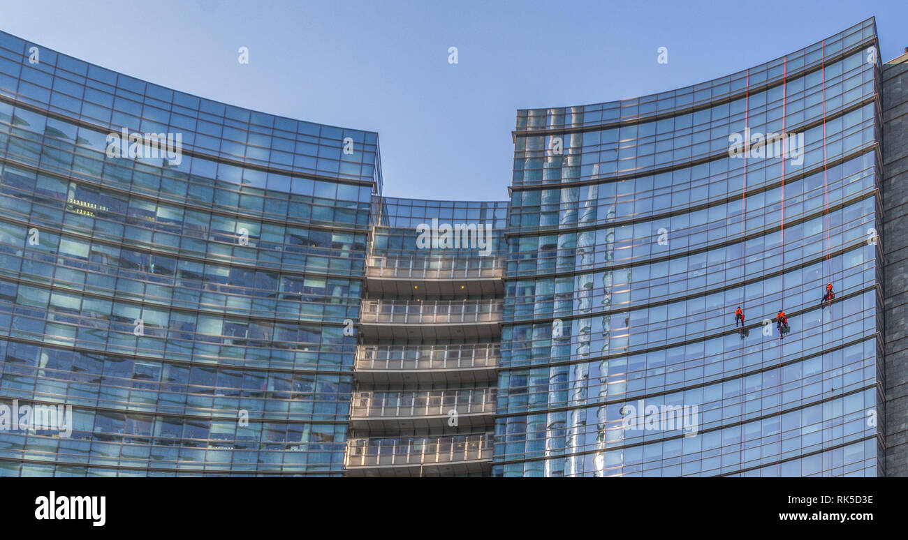 three workers work to clean the windows of a large skyscraper in Milan ...