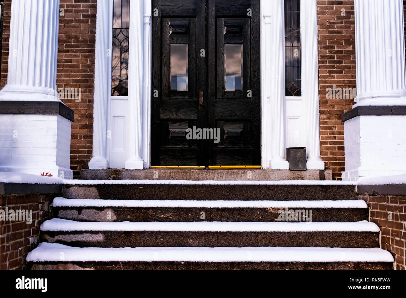 The snow covered steps to an old brick house with white pillars in ...