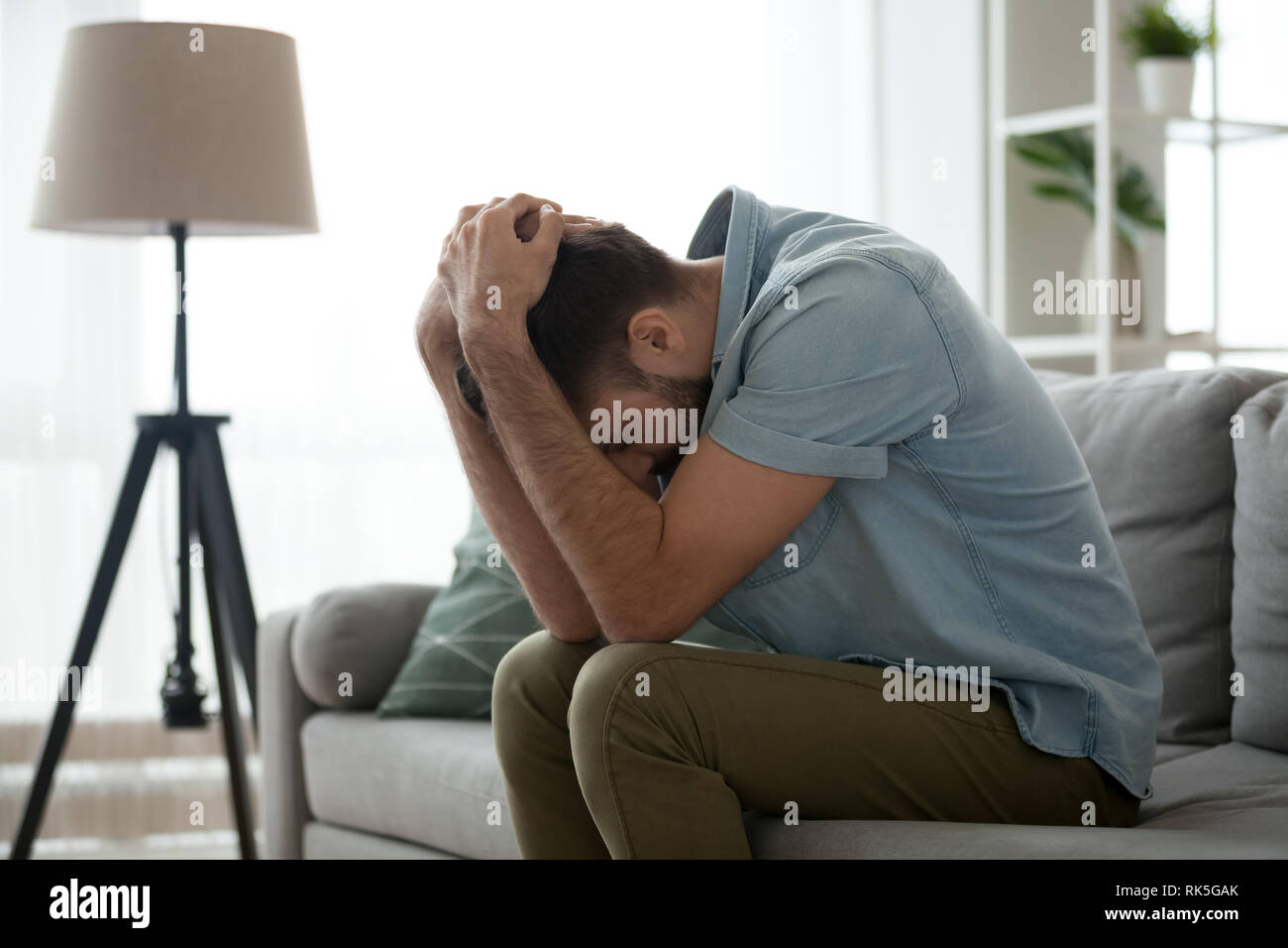 Depressed sad man sitting on couch holding head in hands Stock Photo ...