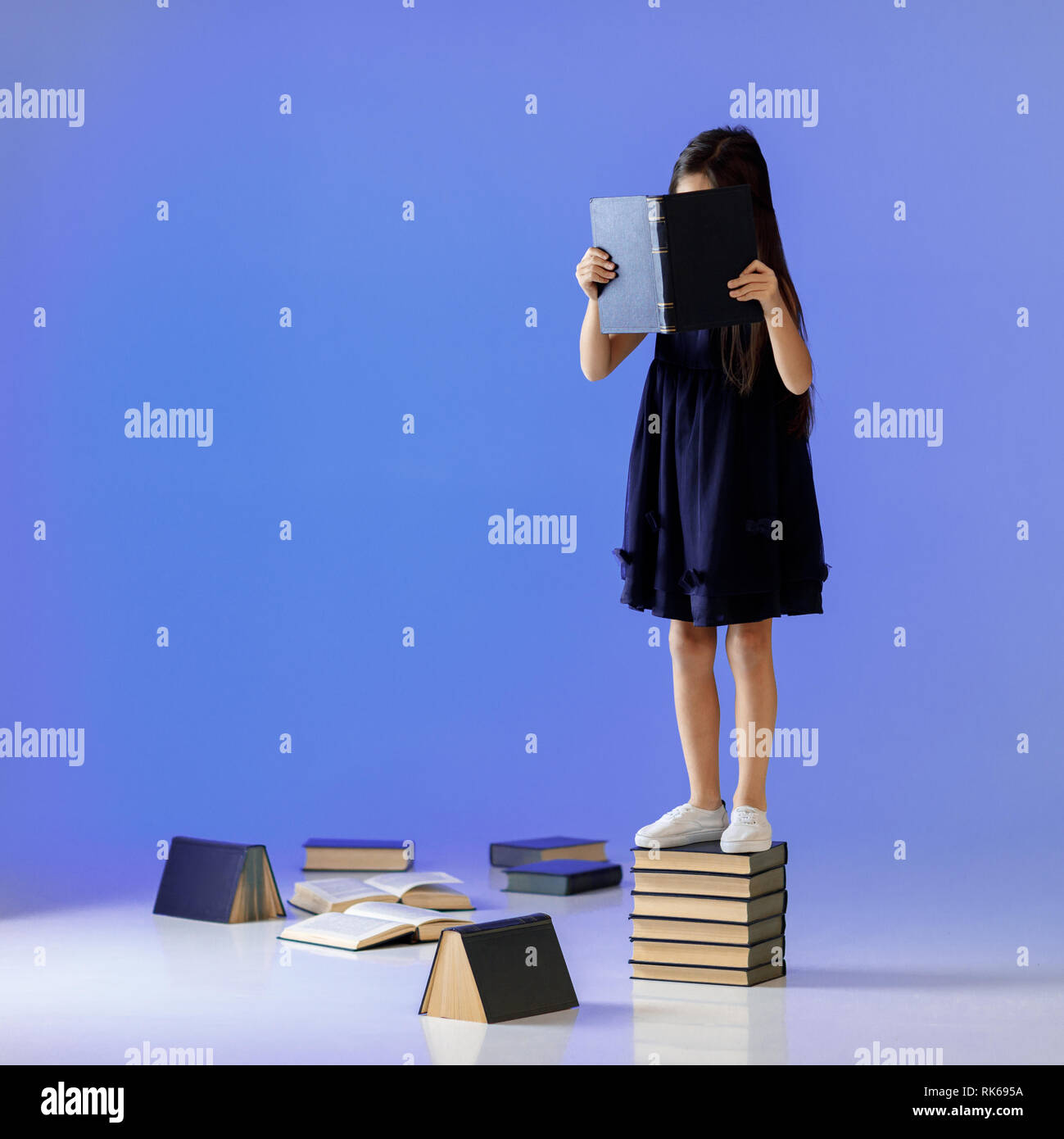 cute little child girl in dark blue dress is reading book and standing ...