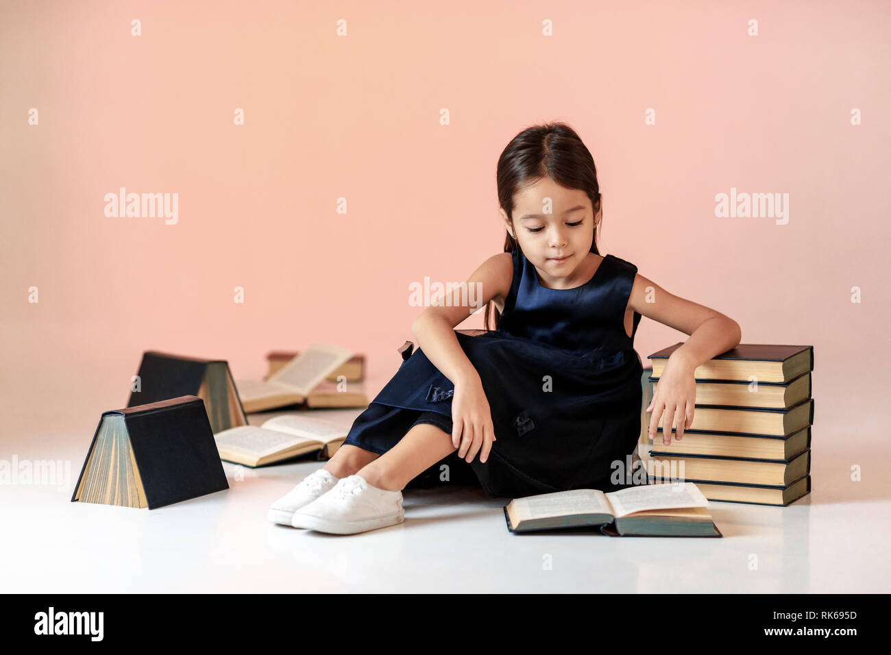 cute little girl in dark blue dress is reading a book. child and a lot ...