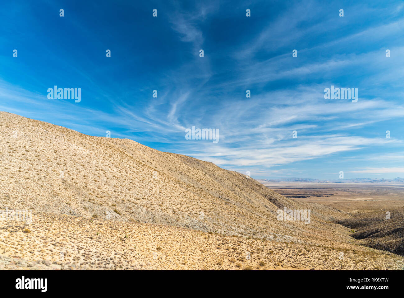 Looking down desert mountainside to valley below under big bright blue ...