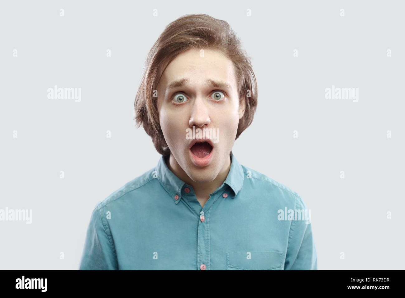 Portrait of shocked handsome long haired blonde young man in blue shirt ...