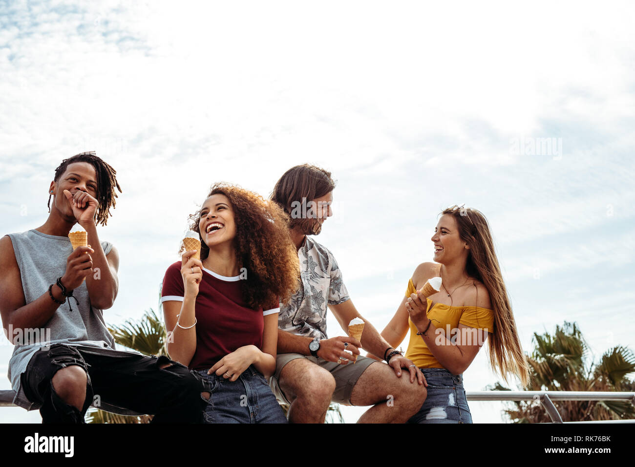 Young men and women leaning to a railing outdoors and enjoying eating ...
