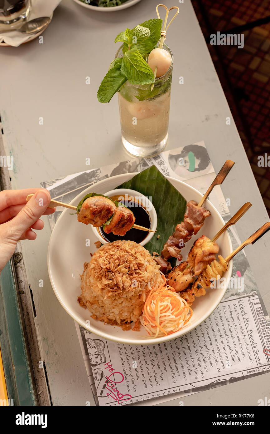 A hand holding a skewer from a meat combo served with fried rice ...