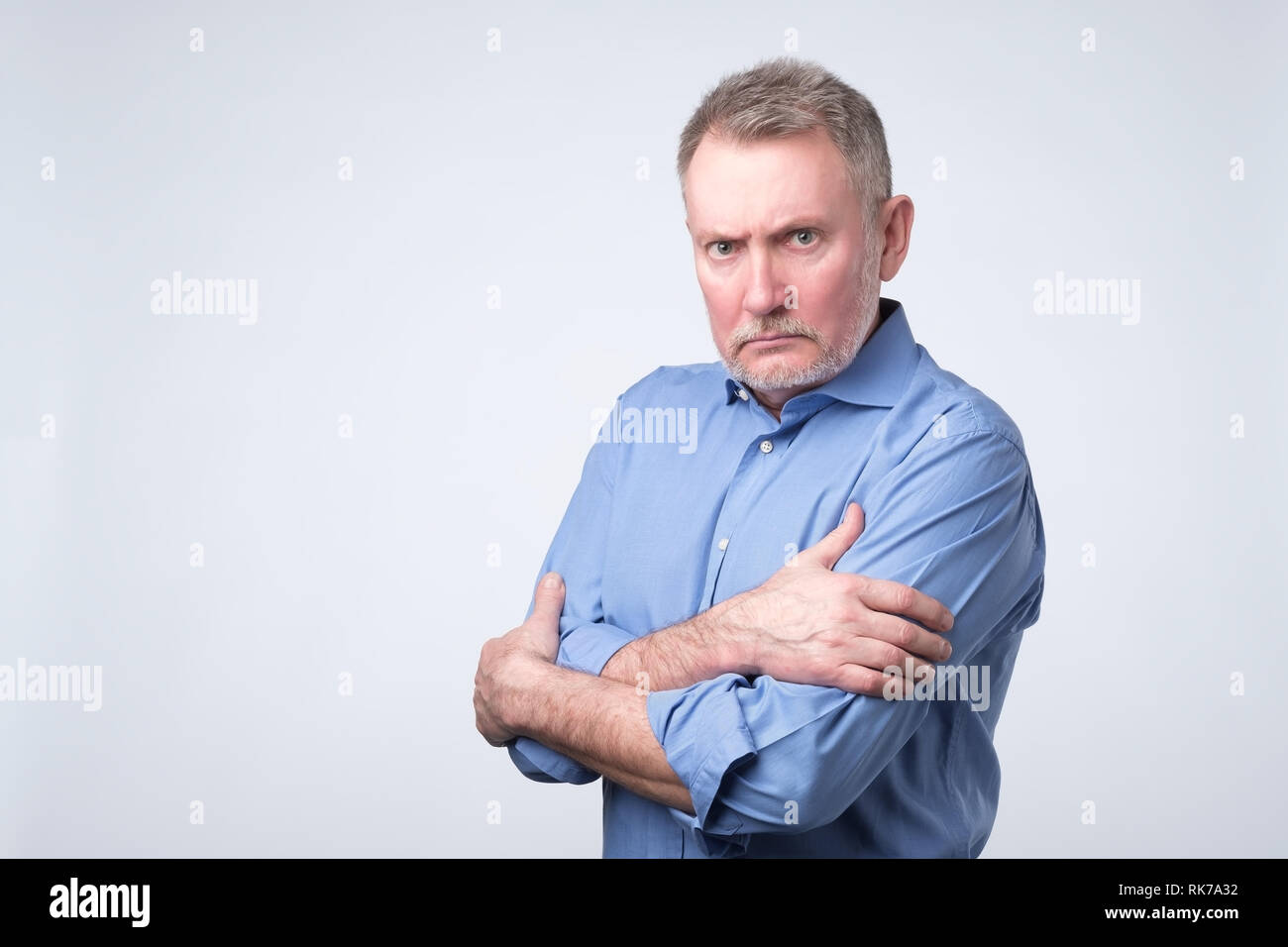 Serious senior man with folded arms and a deadpan expression posing on ...
