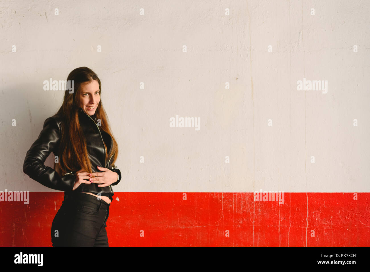 Young millennial woman standing in profile on white and red wall ...