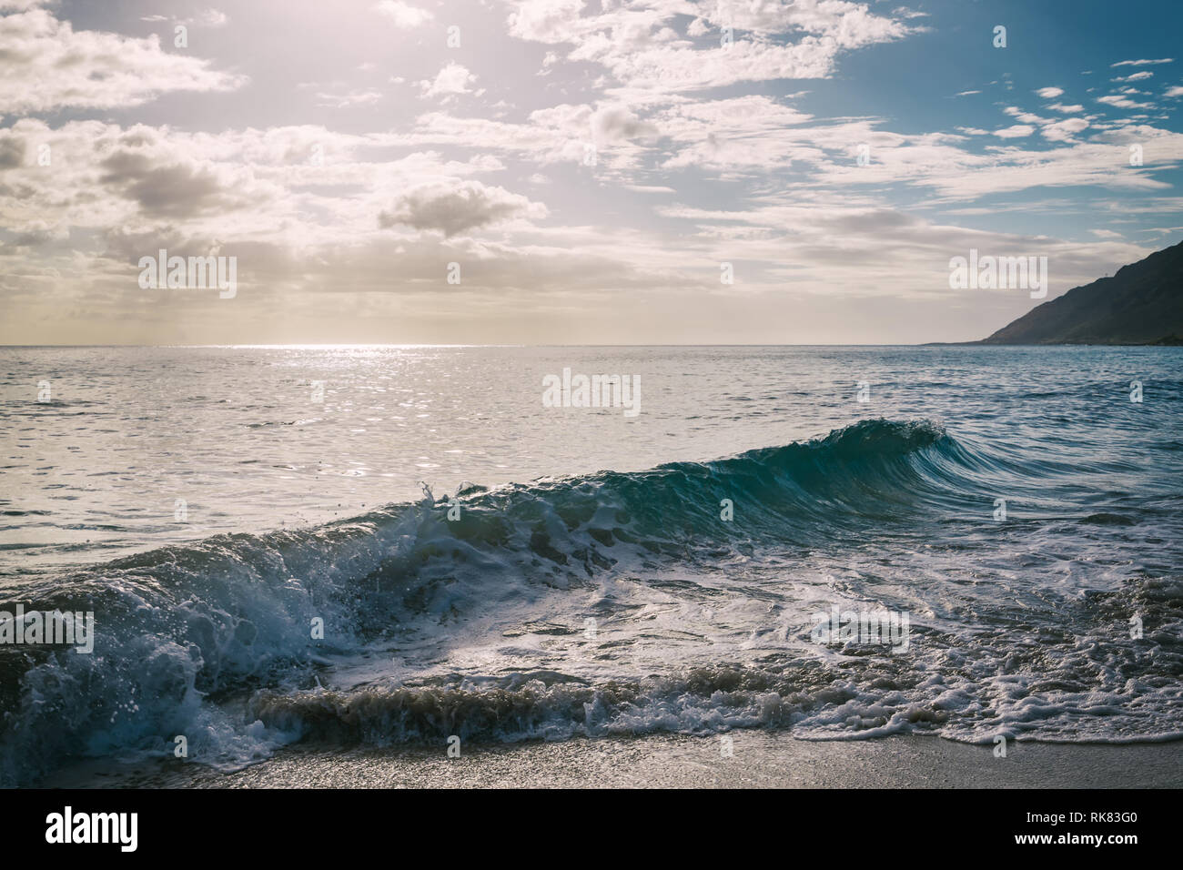 Sun shining through the clouds at sandy beach with waves Stock Photo ...