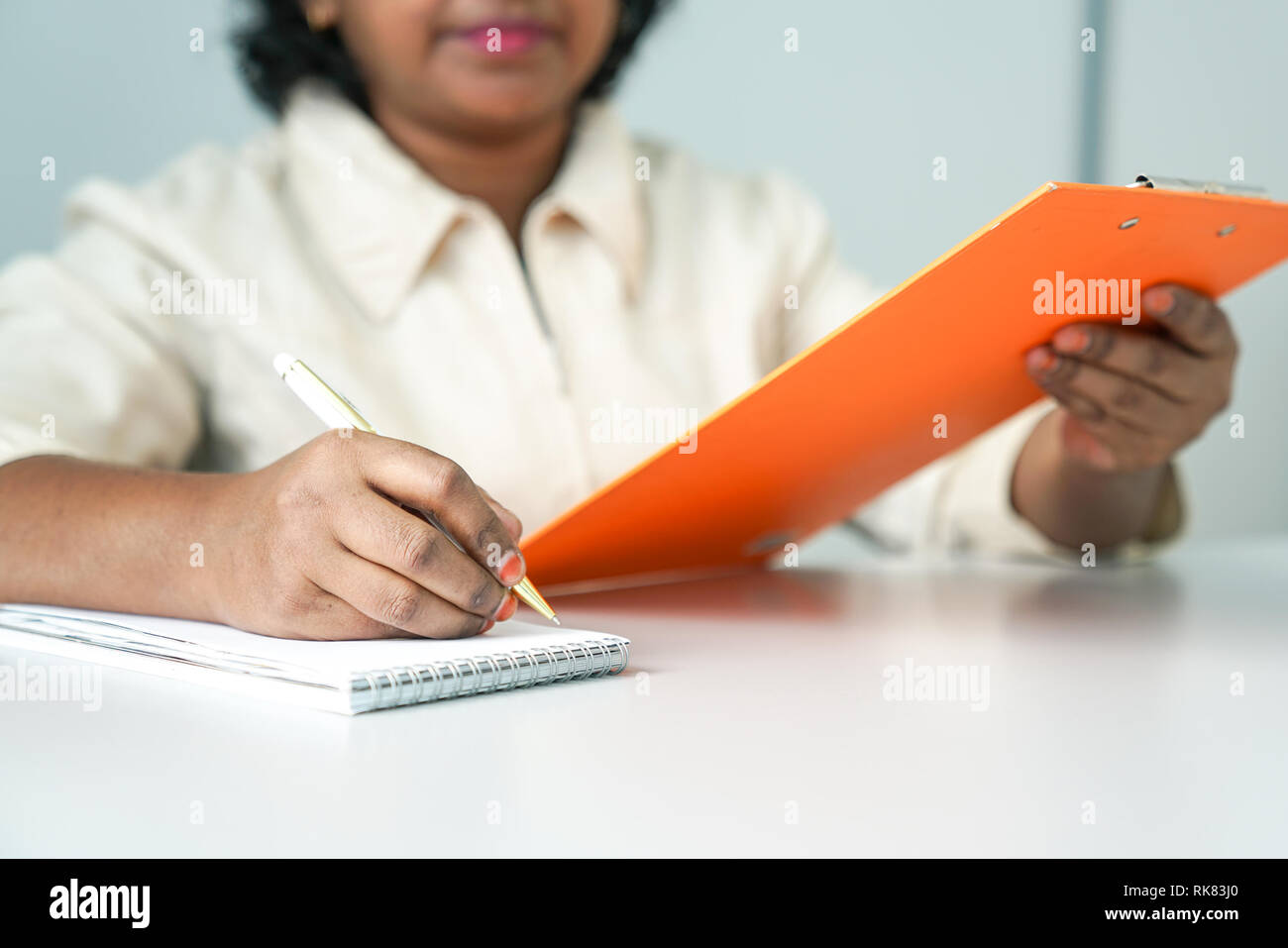 Female Asian conducting meeting or interview with clipboard and writing ...