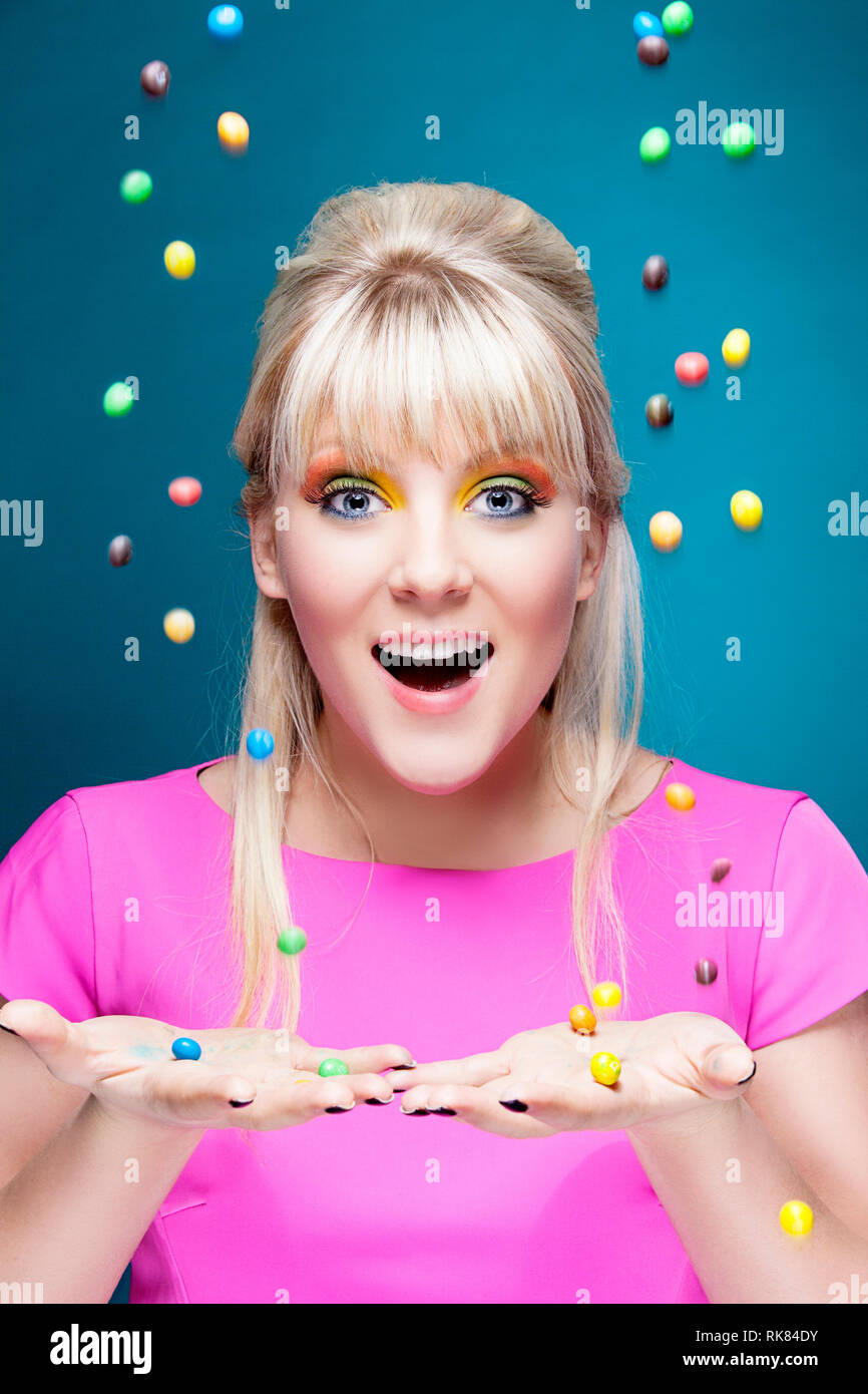 beautiful blond young woman with colorful makeup and many candies falling. studio beauty shot ...