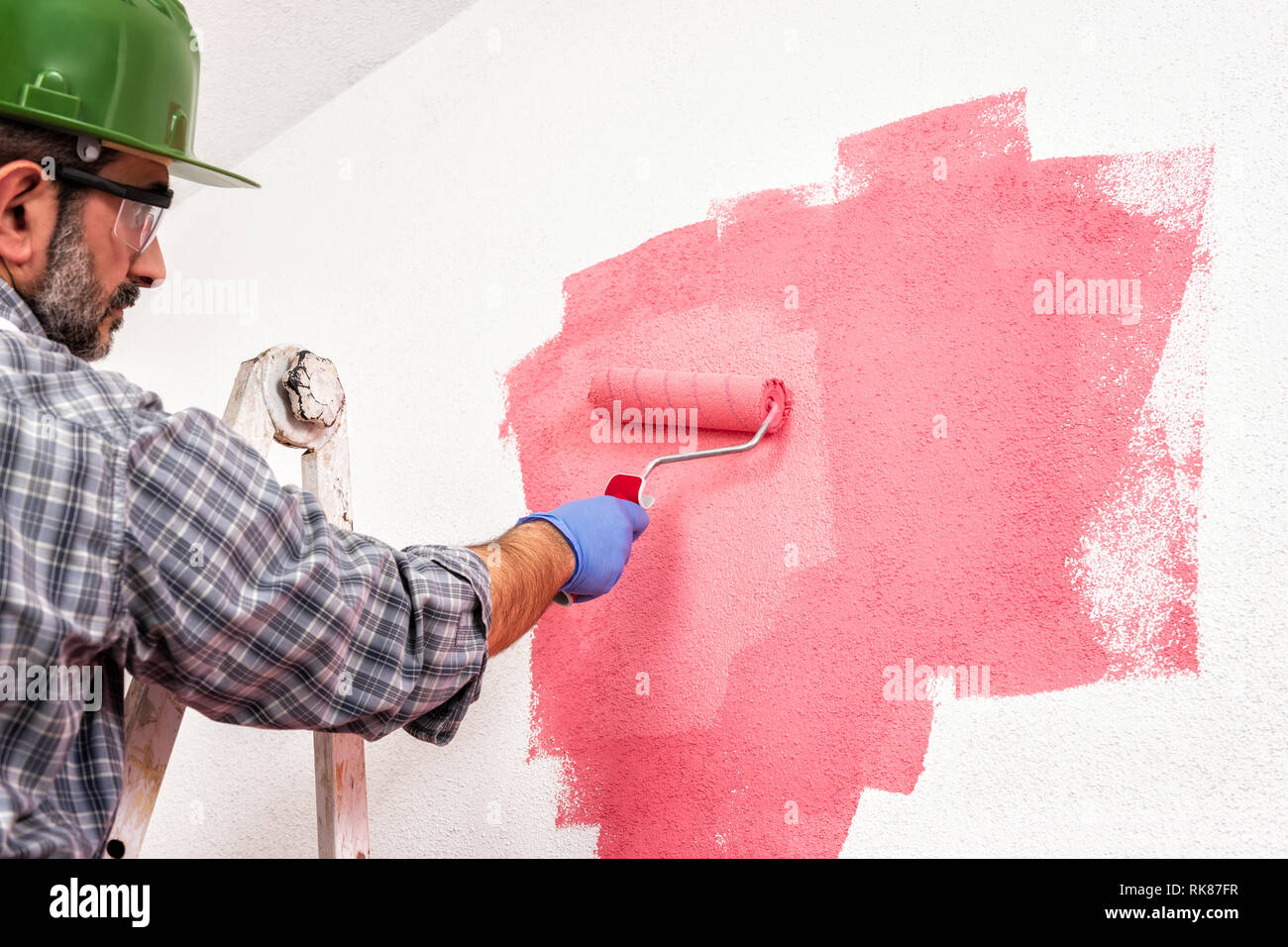 Caucasian house painter worker on a metal ladder, with the roller he ...