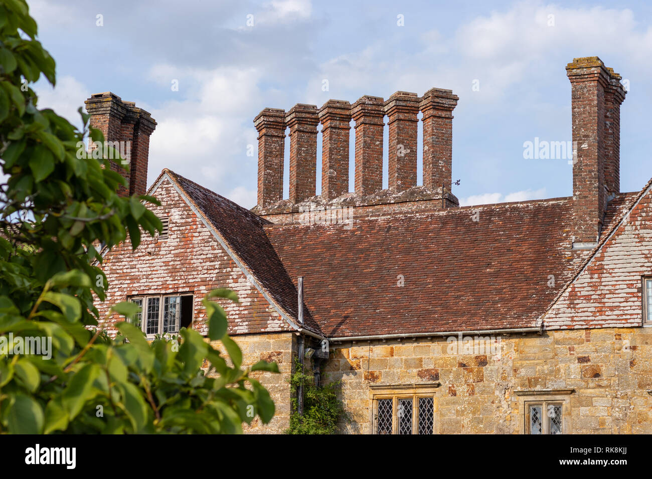 Chimneys on roof of English manor house with blue sky and clouds behind ...