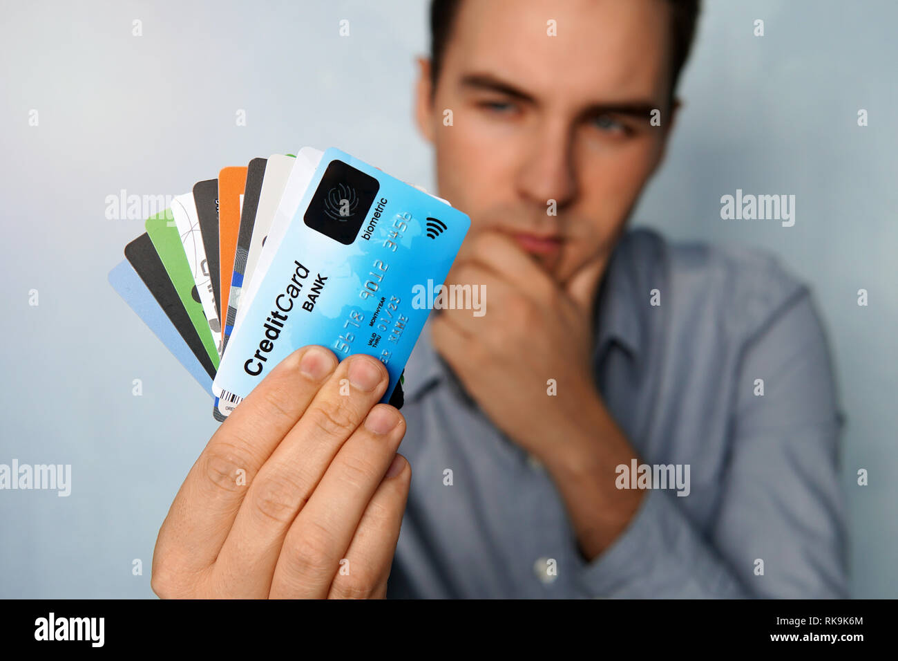 The young man is holding a stop of credit and debit cards in a pensive ...