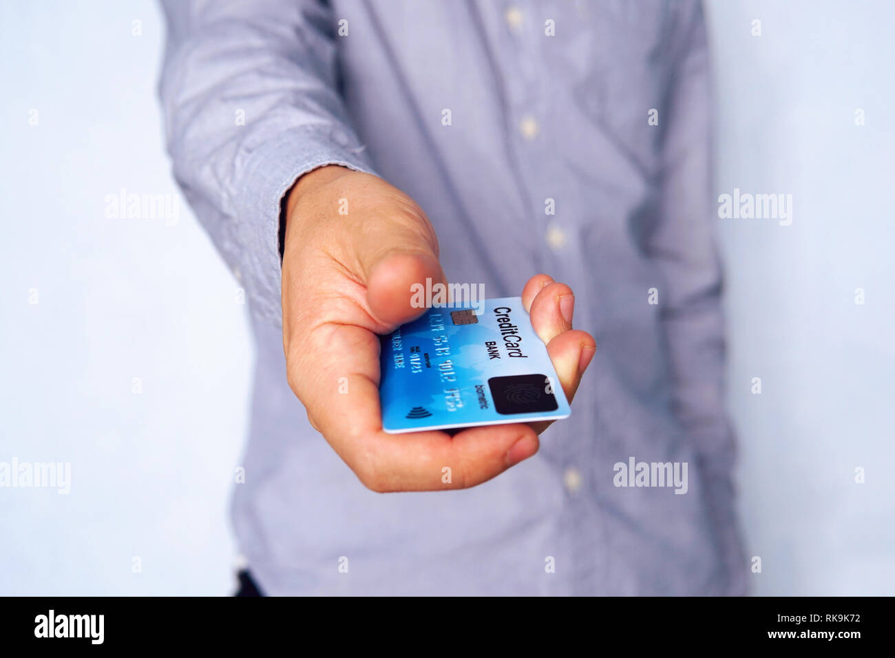 Casual young businessman at blue background giving credit card with ...