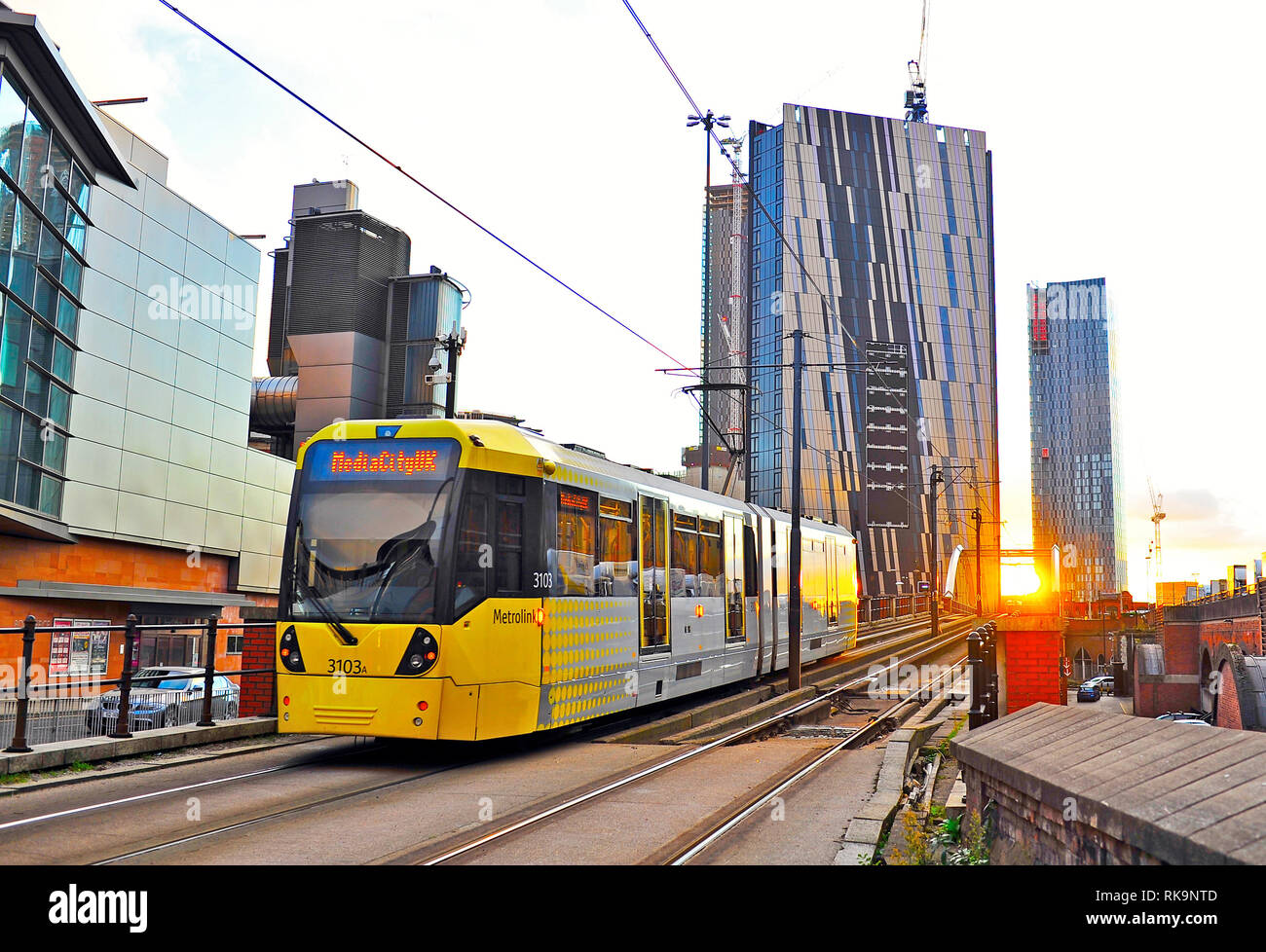 Manchester Metro tram in front of the sun setting between two apartment ...