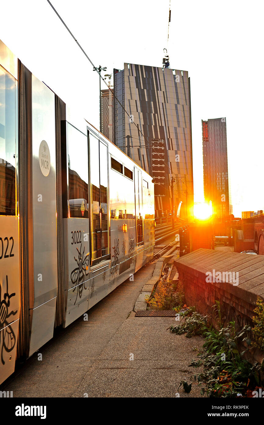 Manchester Metro tram in front of the sun setting between two high rise ...