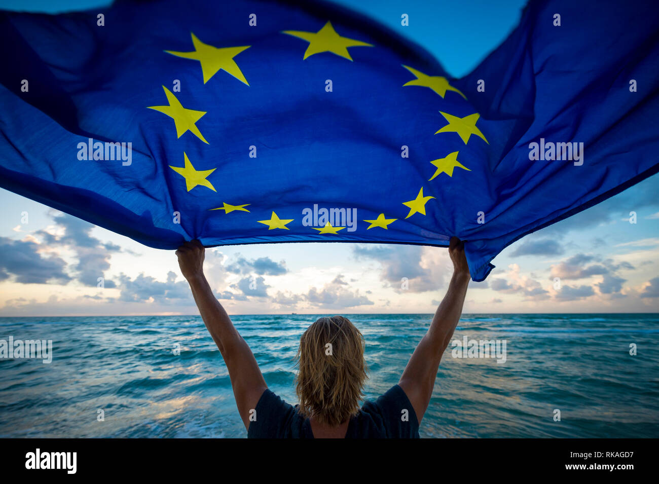 Man holding a fluttering European Union flag flying in bright morning ...
