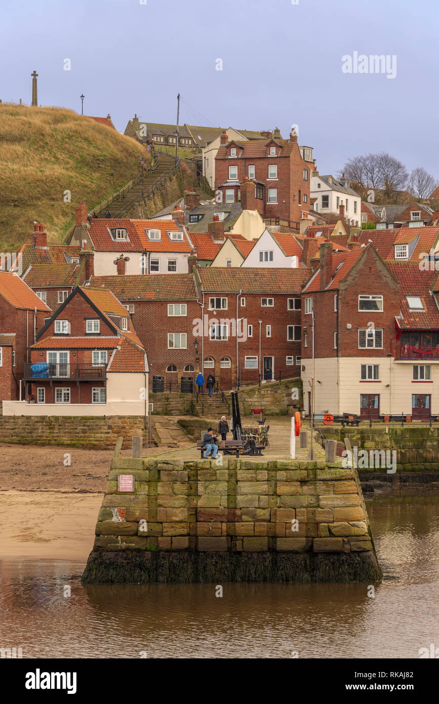 A pier at Whitby jutting out into the harbour. Houses are stacked up ...